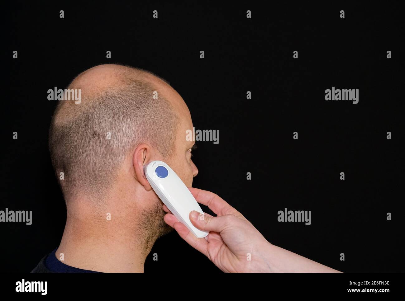 Adult male having his temperature taking with a digital ear thermometer ...