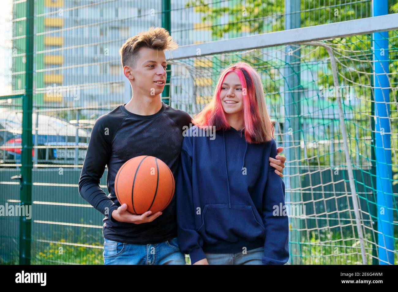 Portrait of guy and teenage girl hugging on basketball court with ball ...