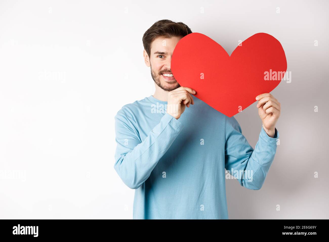 Smiling handsome man holding romantic red heart over half of face ...