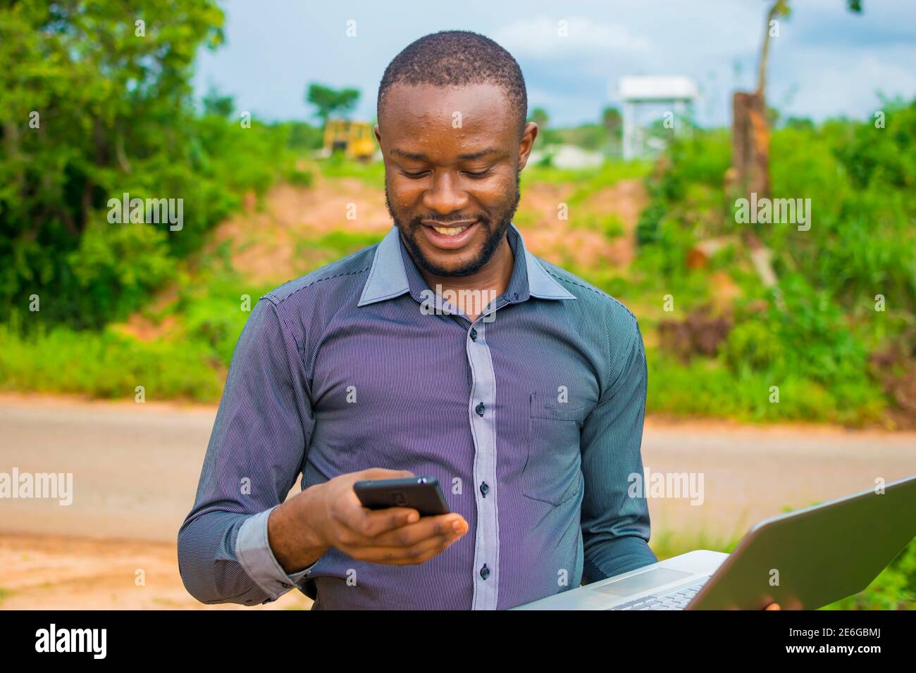 young black man using his laptop and his smartphone on his farmland ...