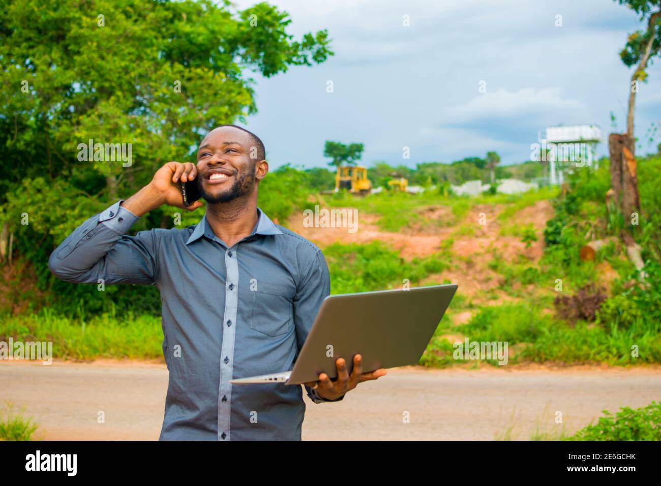 young black man using his laptop and his smartphone on his farmland ...