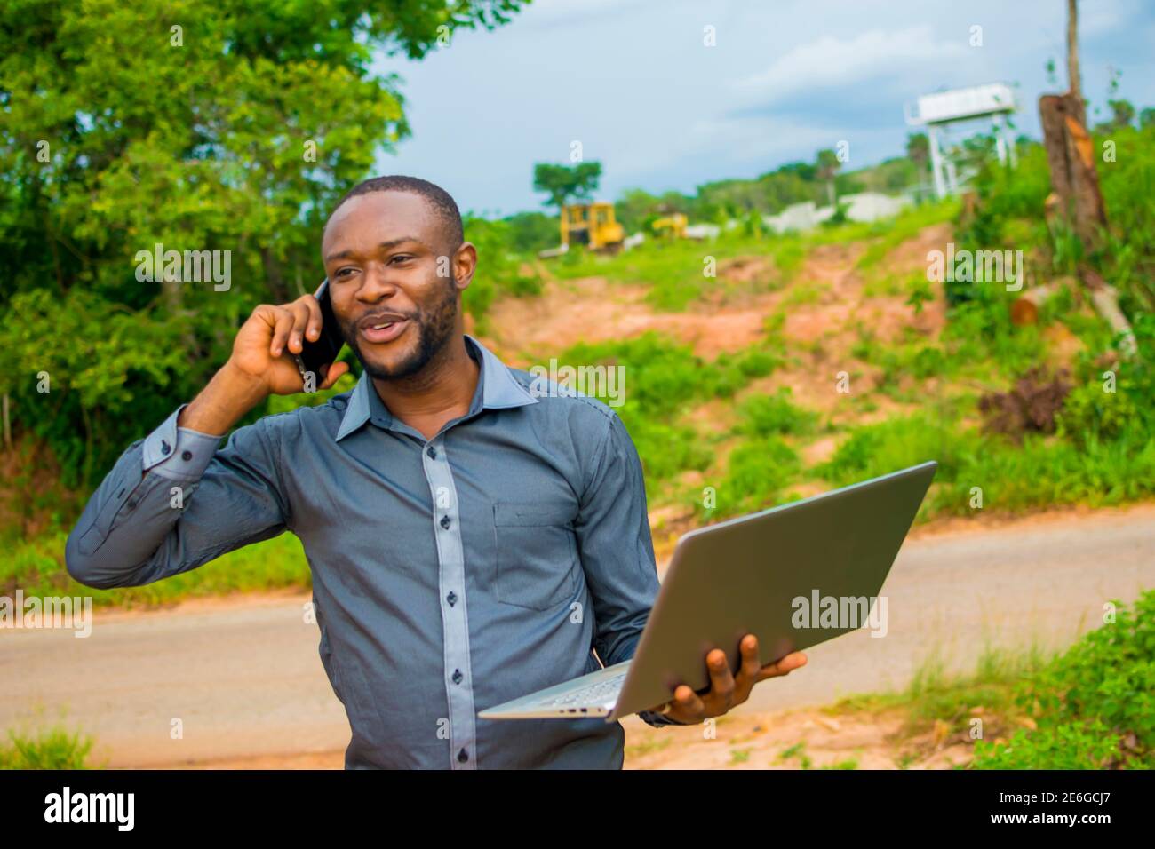 young black man using his laptop and his smartphone on his farmland ...