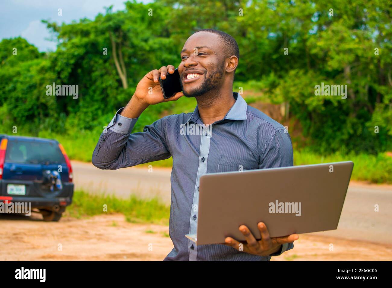 young black man using his laptop and his smartphone on his farmland ...