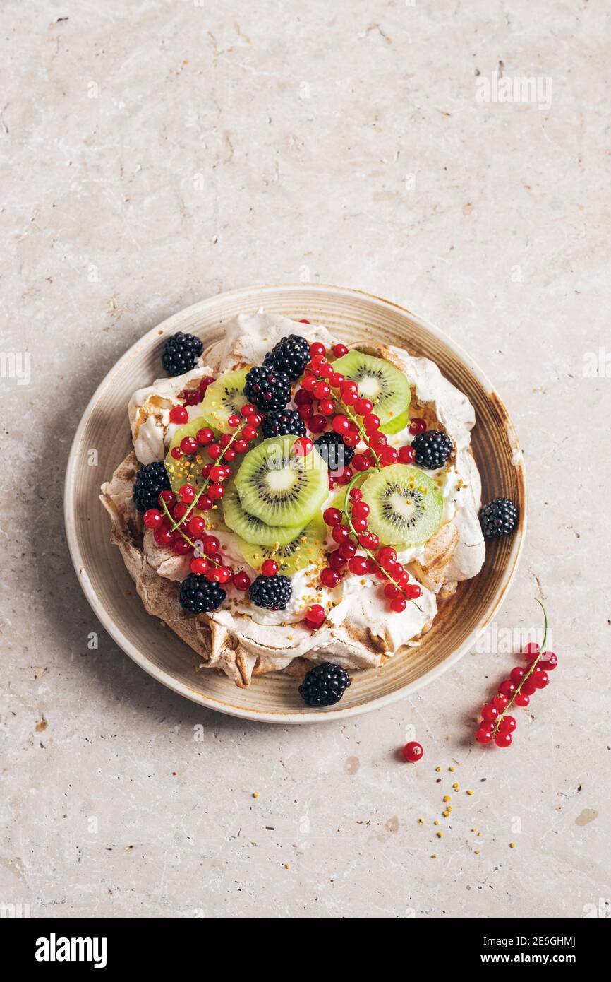 Cinnamon pavlova with berries and kiwi on a natural stone textured ...