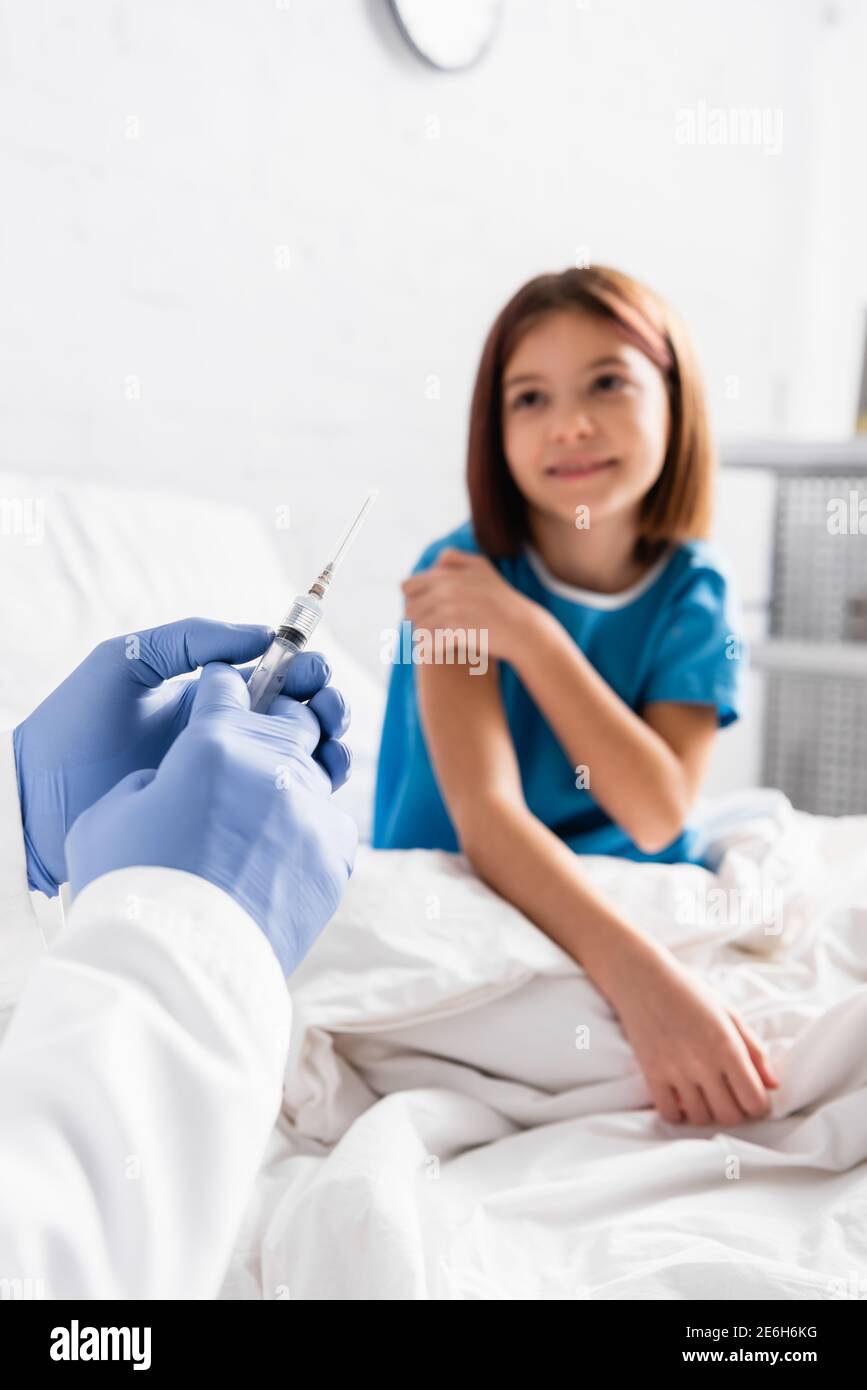 pediatrician holding syringe near smiling child sitting on bed Stock ...