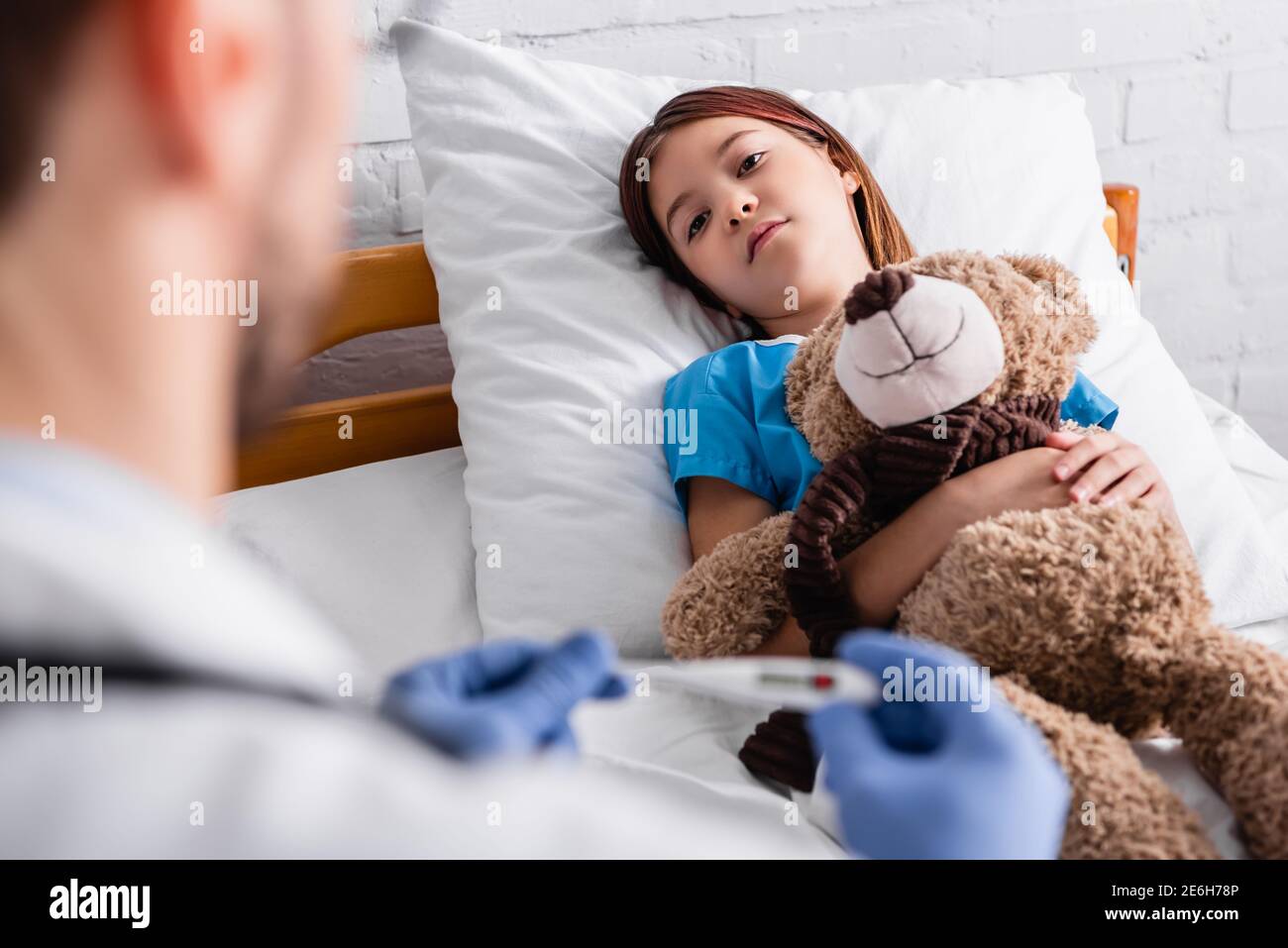 sick child lying in bed with teddy bear near pediatrician with ...