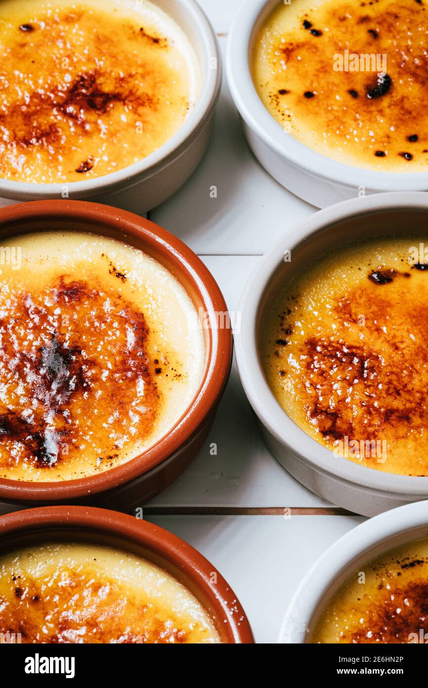 Close up of multiple ramekins of creme brulee on a white tile ...