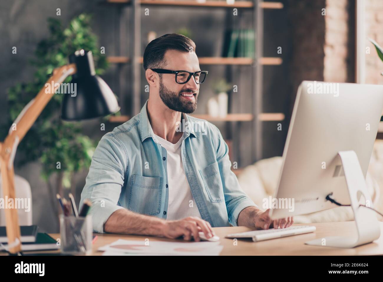 Photo portrait of smiling guy browsing internet on desktop at table in ...