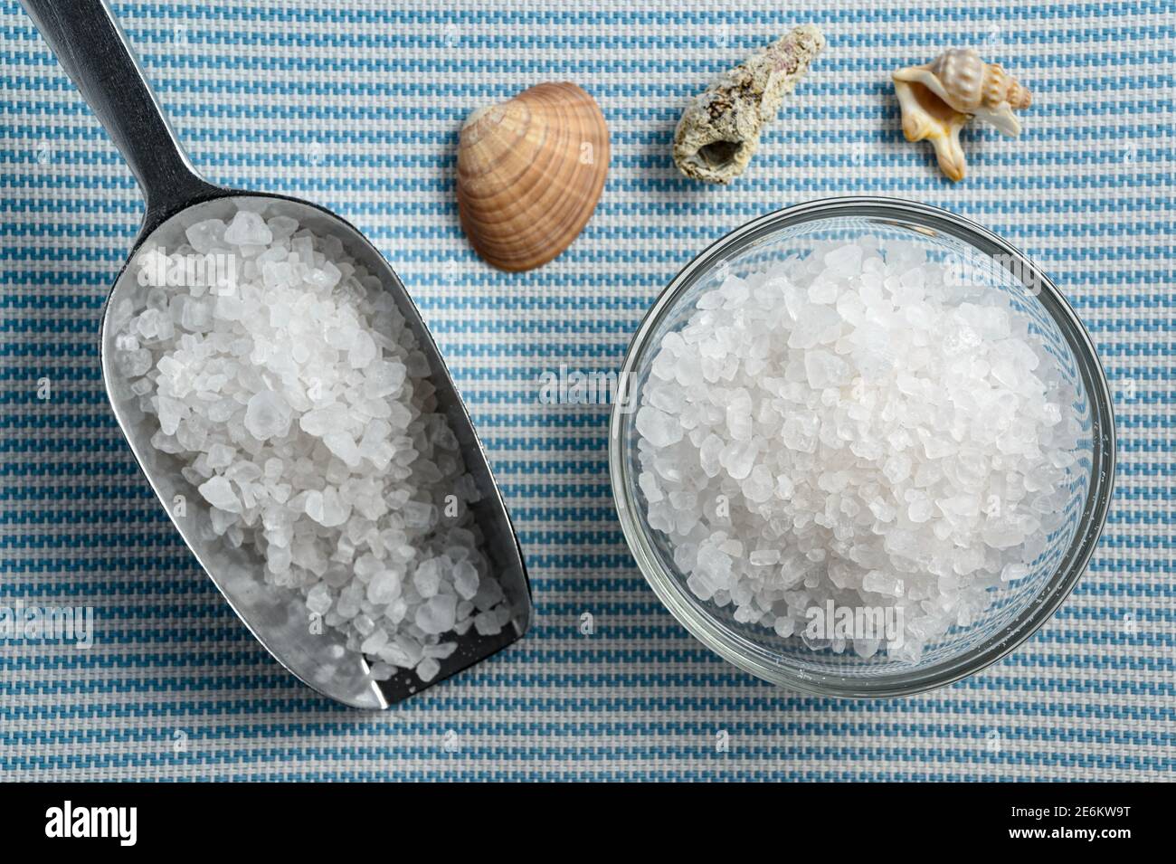 Metallic scoop and glass bowl full of sea salt on white and blue ...