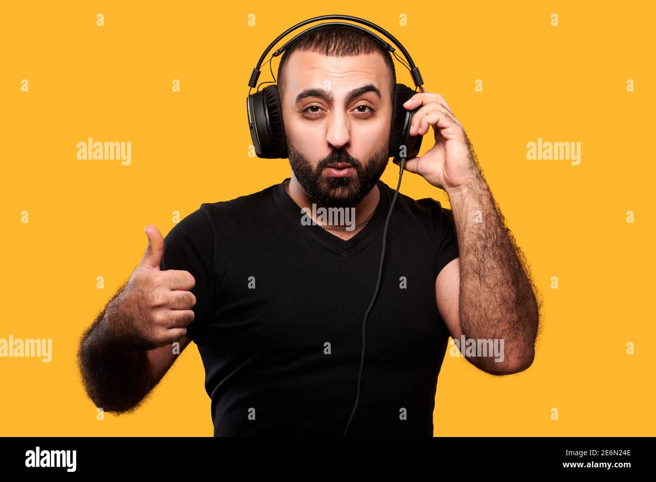 Young arabic dj with beard listening to music in headphones and showing ...