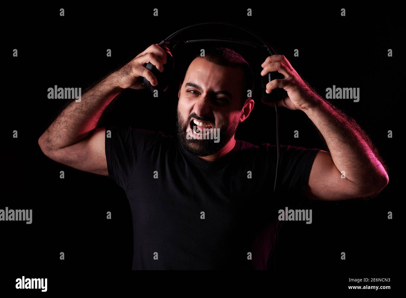 Angry screaming bearded arabic musician dj tearing headphones on black ...