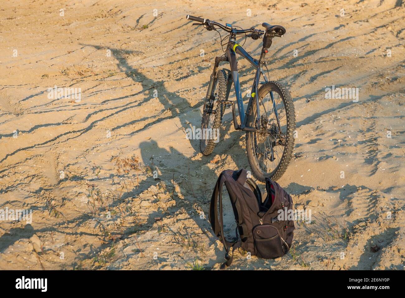 A mountain bike is standing on the sand, and a black backpack is lying ...