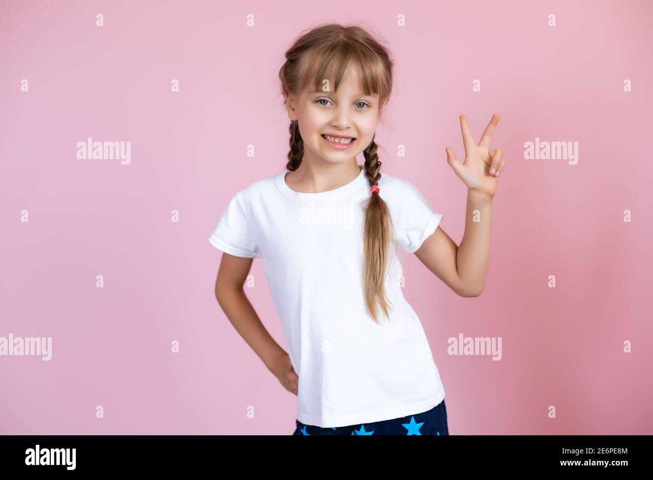 Pretty little girl in a white t-shirt smiling on a pink background ...