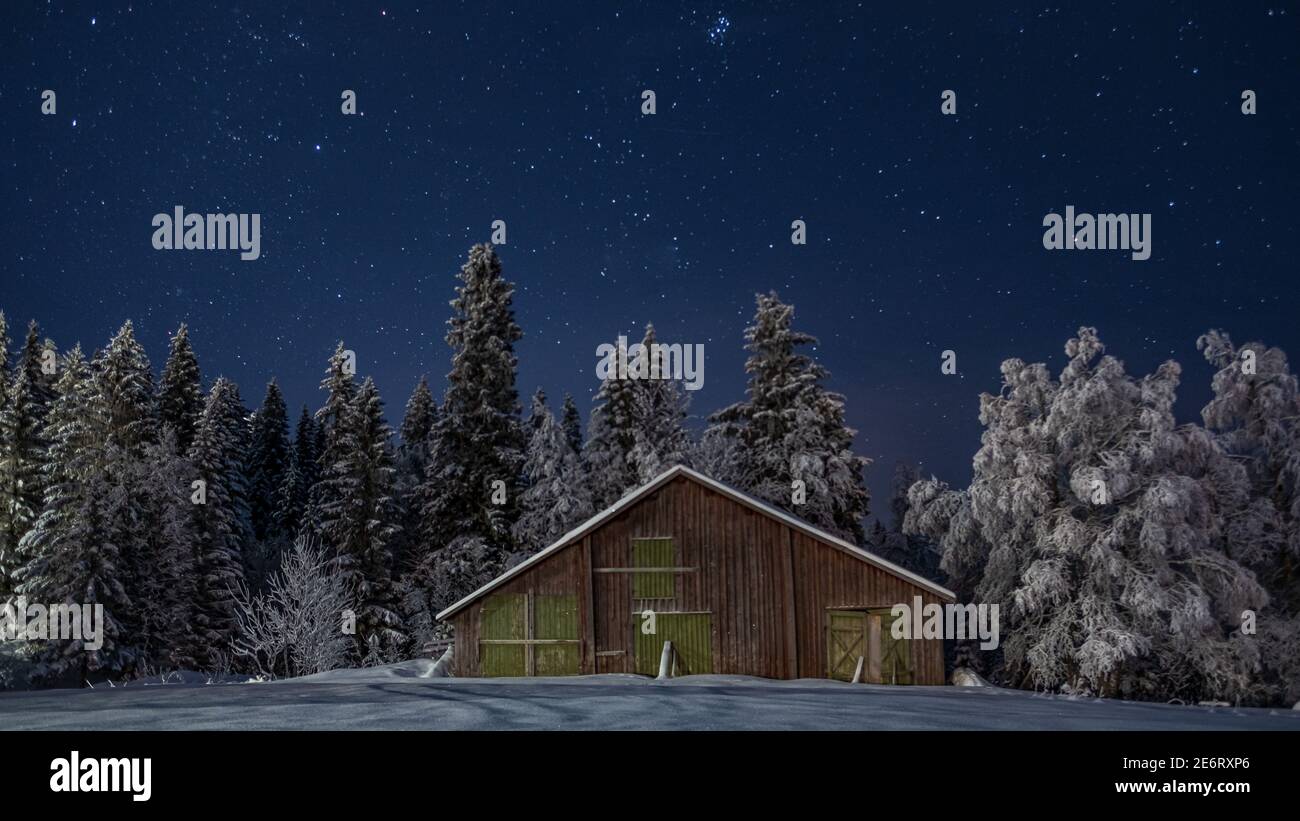Small wooden house in the scenic winter forest on the starry night sky ...
