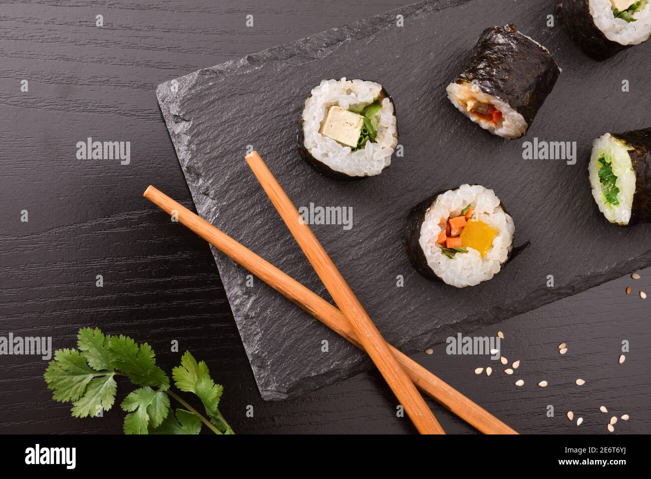 Detail of assorted sushi maki on slate plate and chopsticks on black wooden table. Top view ...