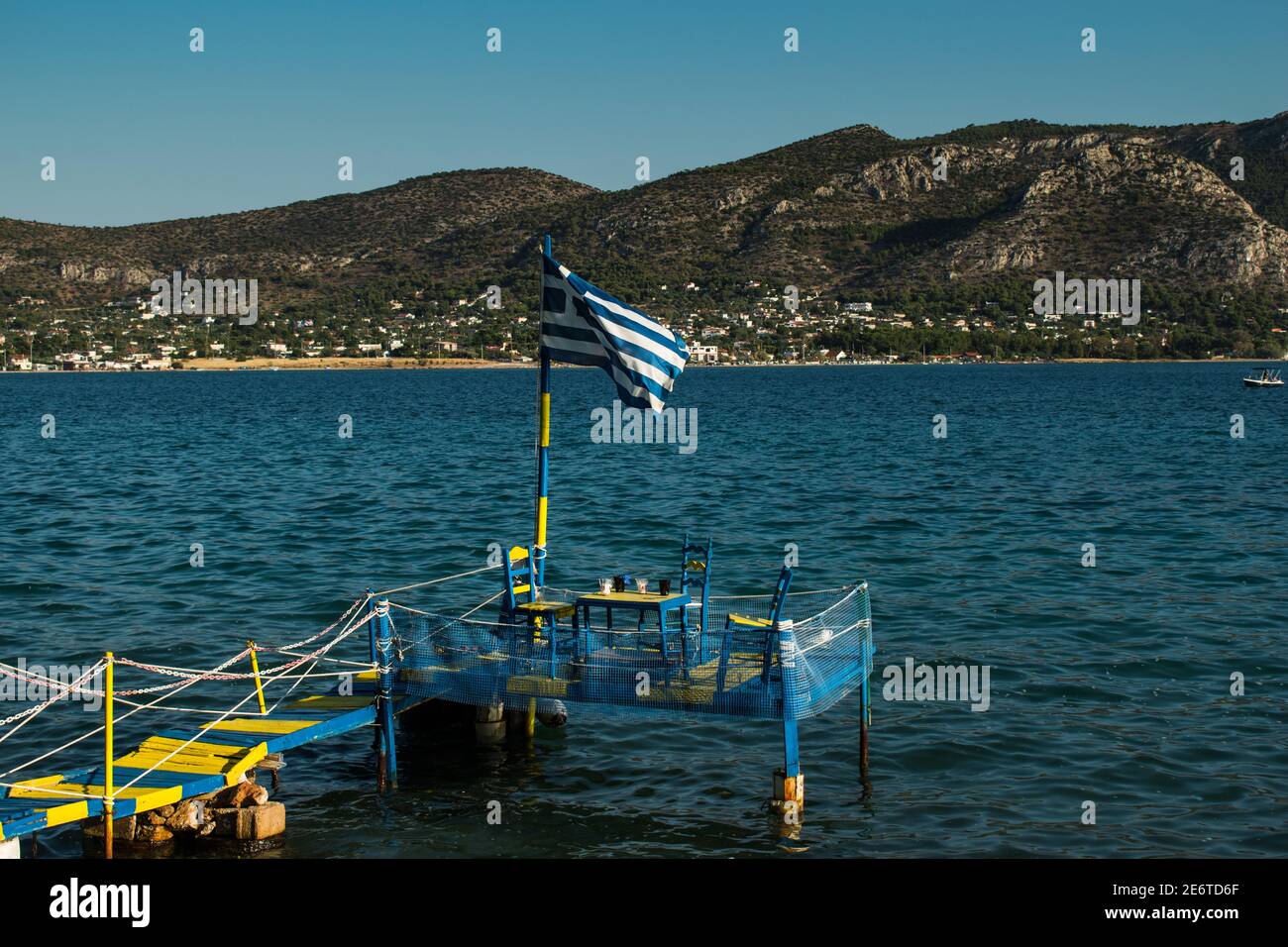 View of a Greek flag waves at a Wooden platform over the sea water ...