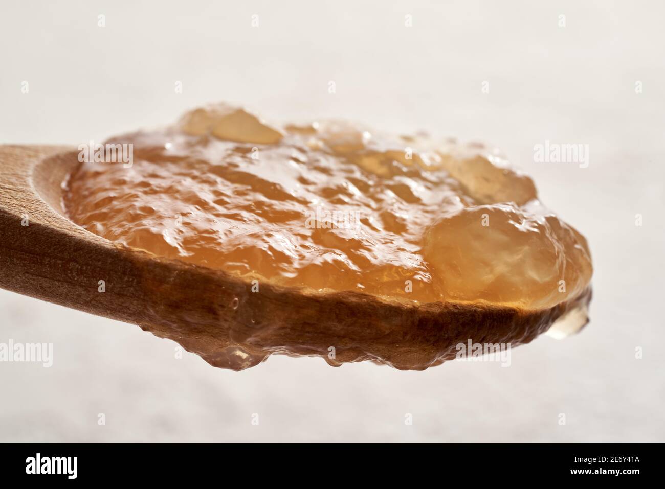 Cooled congealed beef bone broth on a wooden spoon against a white ...
