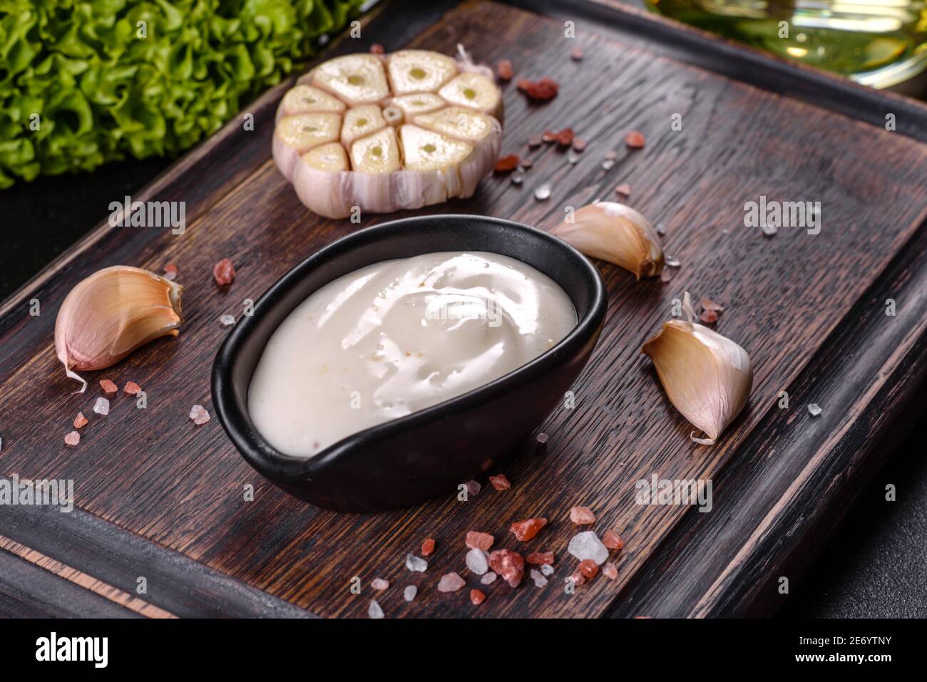 Garlic sauce in a ceramic black sauce with greenery on a wooden cutting ...