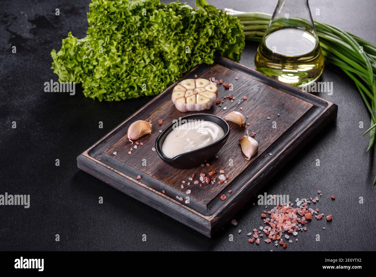 Garlic sauce in a ceramic black sauce with greenery on a wooden cutting ...