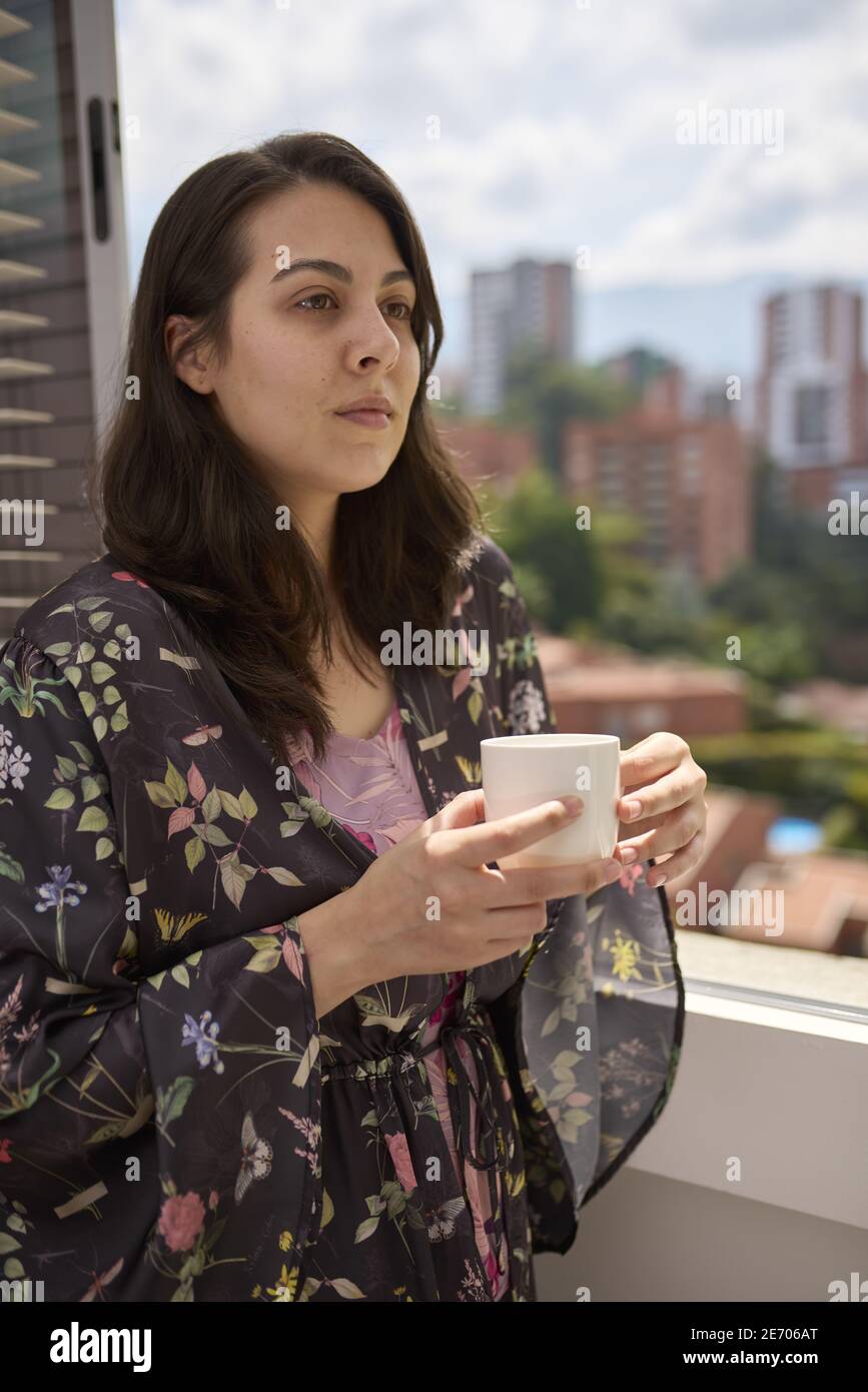 An attractive Hispanic woman in robe enjoying a morning coffee in a ...