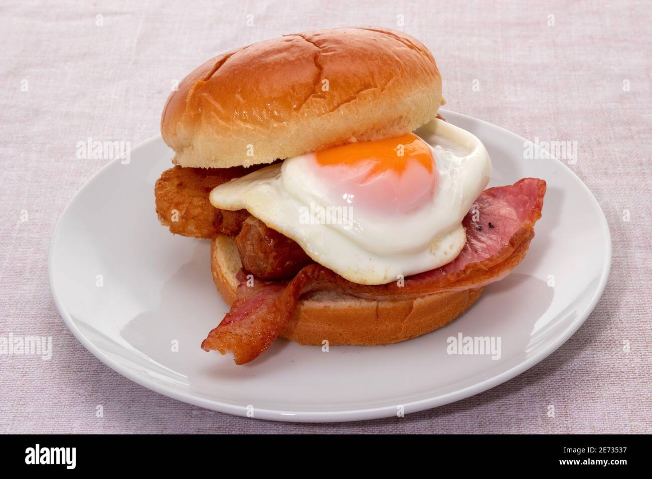 Breakfast brioche roll with a fried egg, hash brown, sausage, and bacon ...