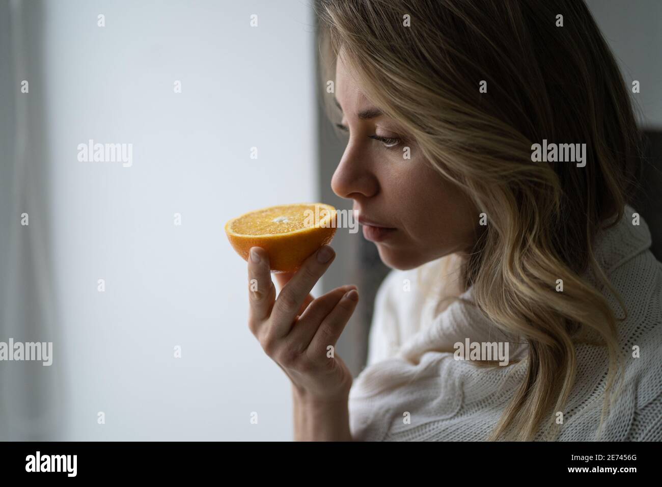 Sick woman trying to sense smell of half fresh orange, has symptom of ...