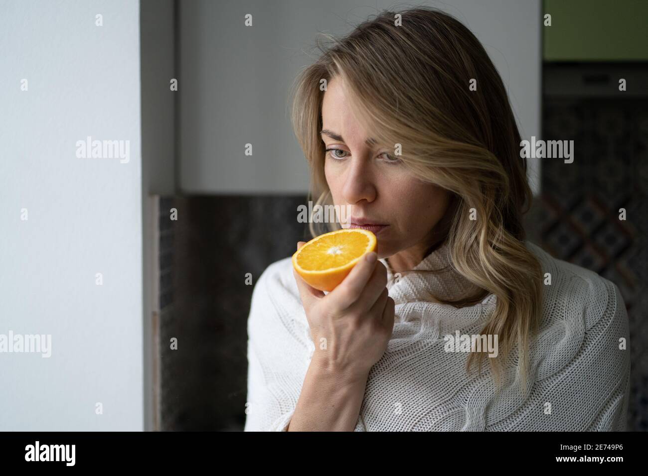 Sick woman trying to sense smell of half fresh orange, has symptom of ...