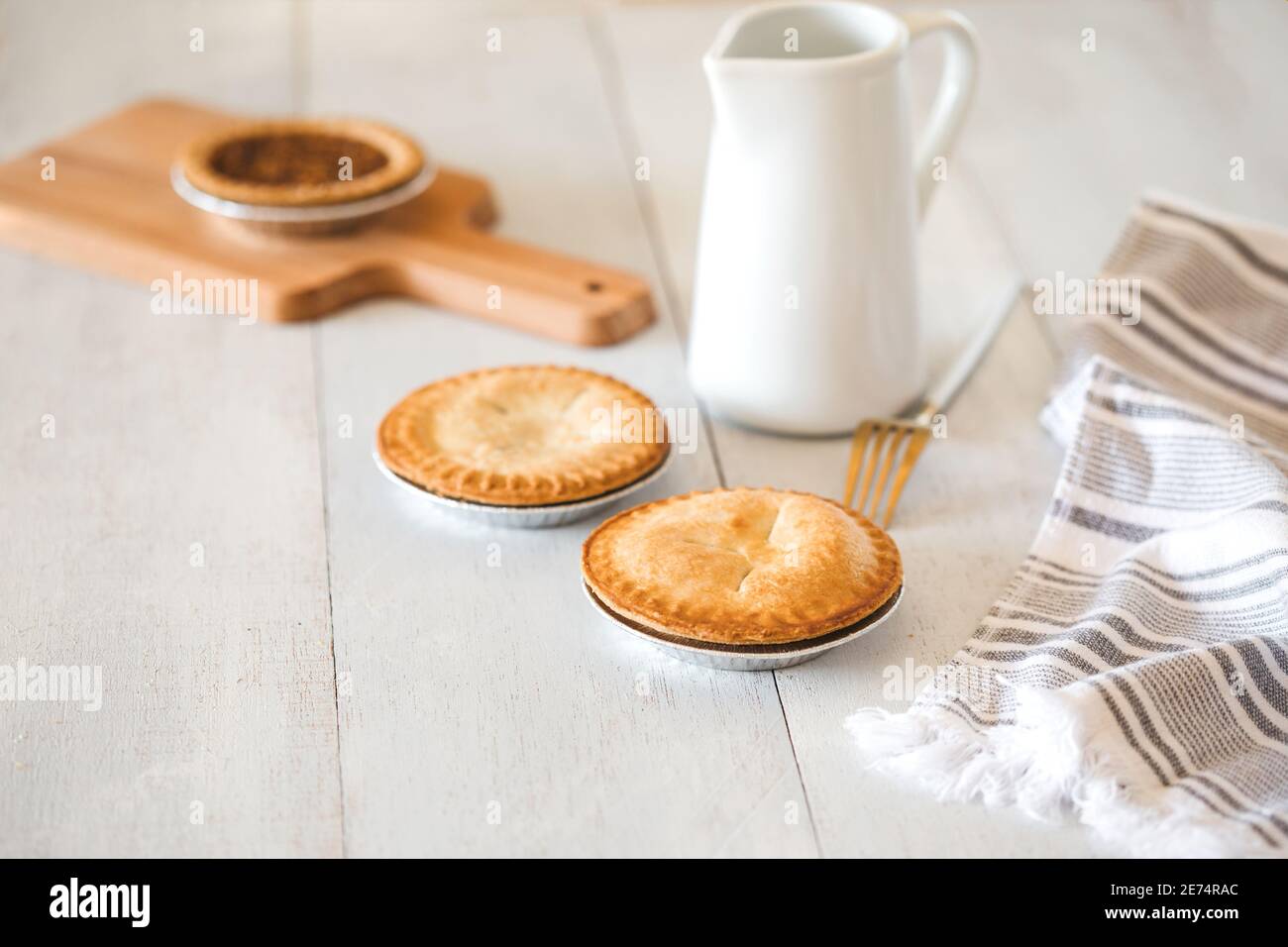 Three mini pies straight from the oven on white wooden table with milk ...