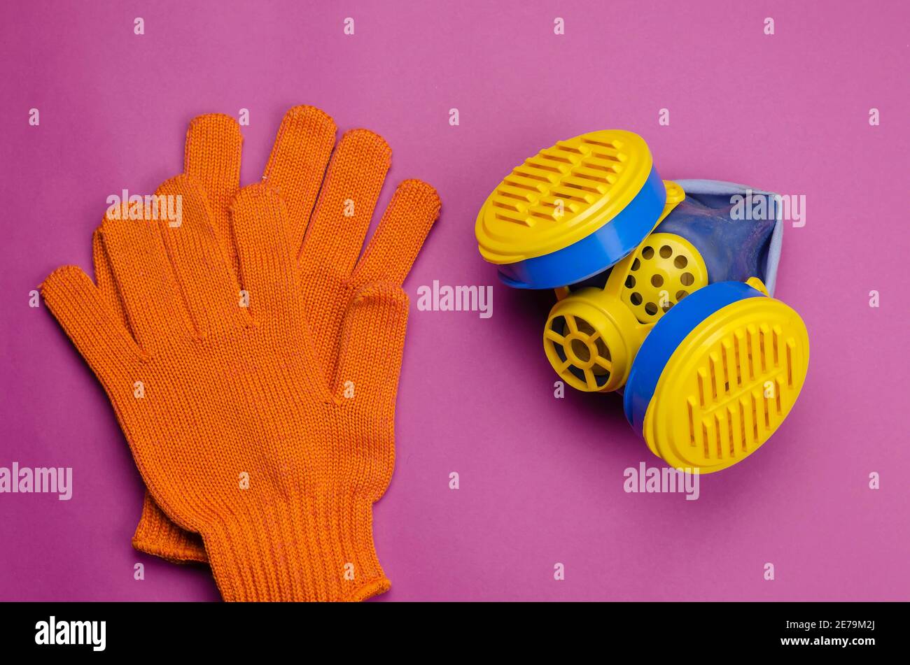 Yellow and blue respirator and protective gloves on a pink background ...