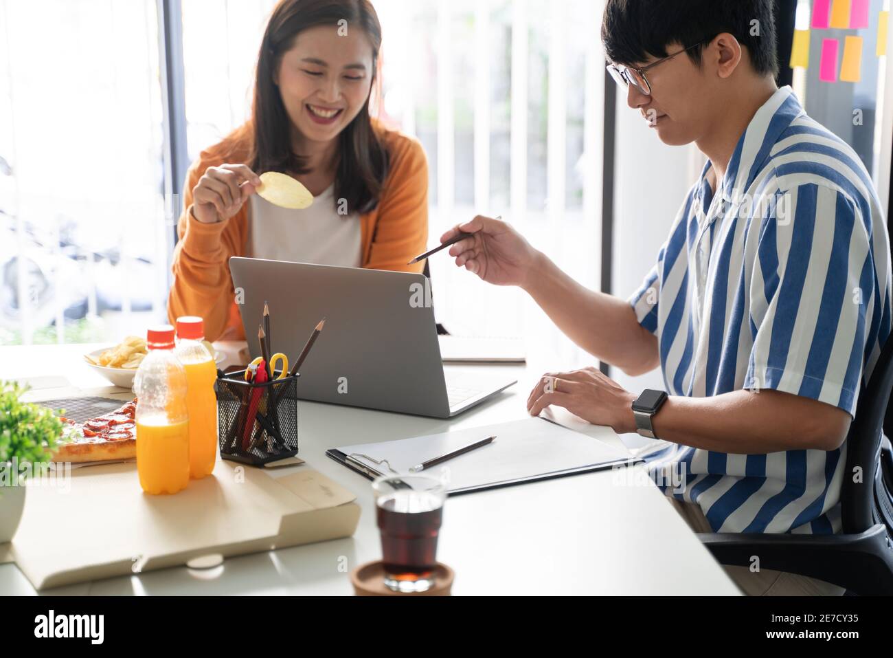 Friendly asian business team colleagues eating pizza and potato chips ...