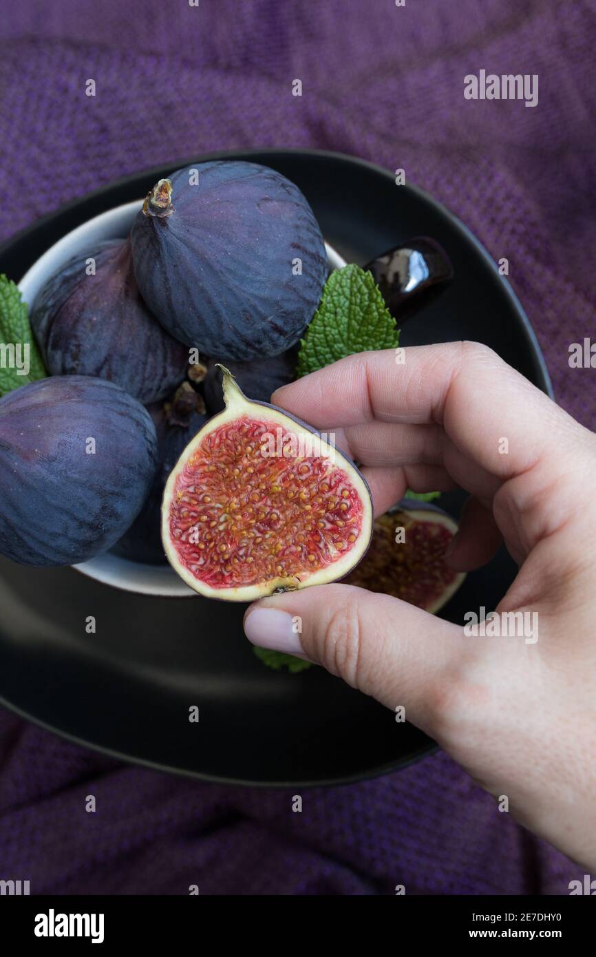 Closeup view of a woman hand taking a halved fig full of colorful seeds ...