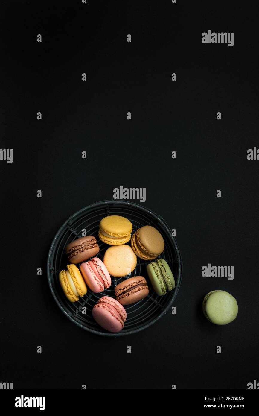 Circled wire tray full of tasty macaroons on a black background. A mint ...