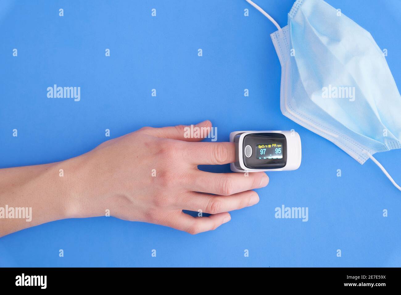 Pulse oximeter on a finger and a face mask on a blue background Stock ...