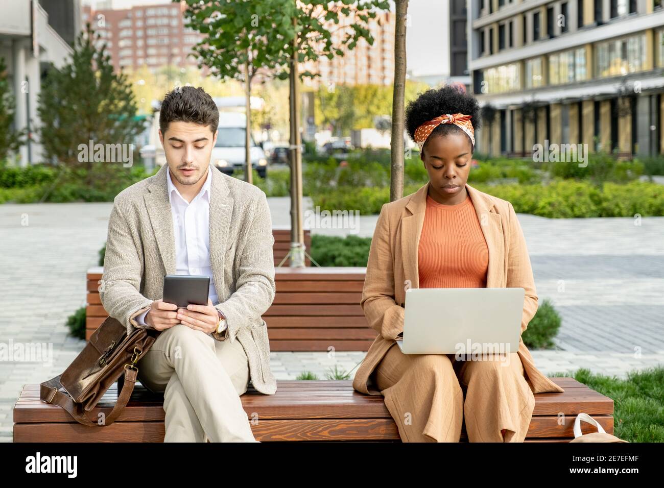 Two young business people sitting on bench and working online on ...