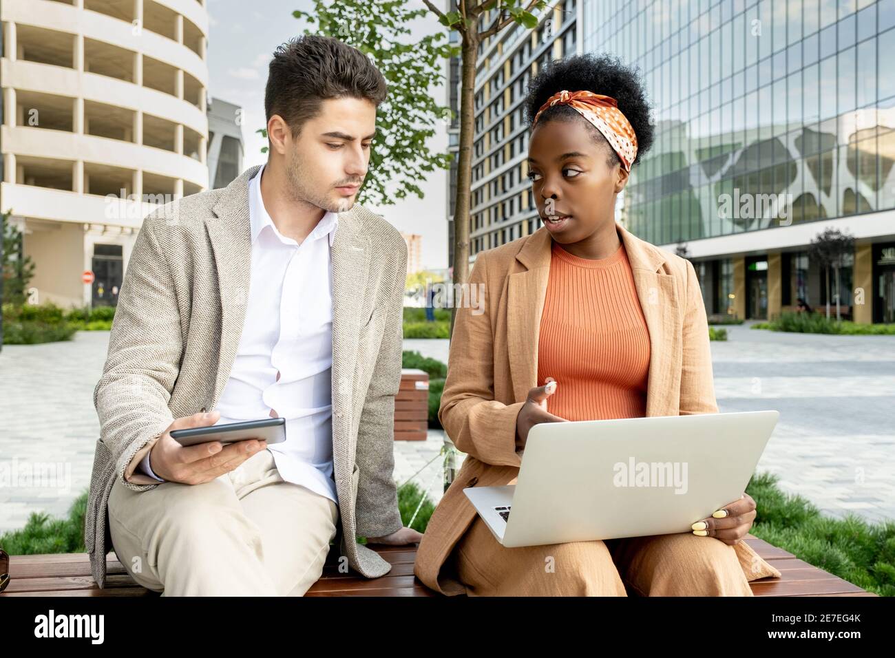 Two business partners sitting on bench with laptop and working online ...