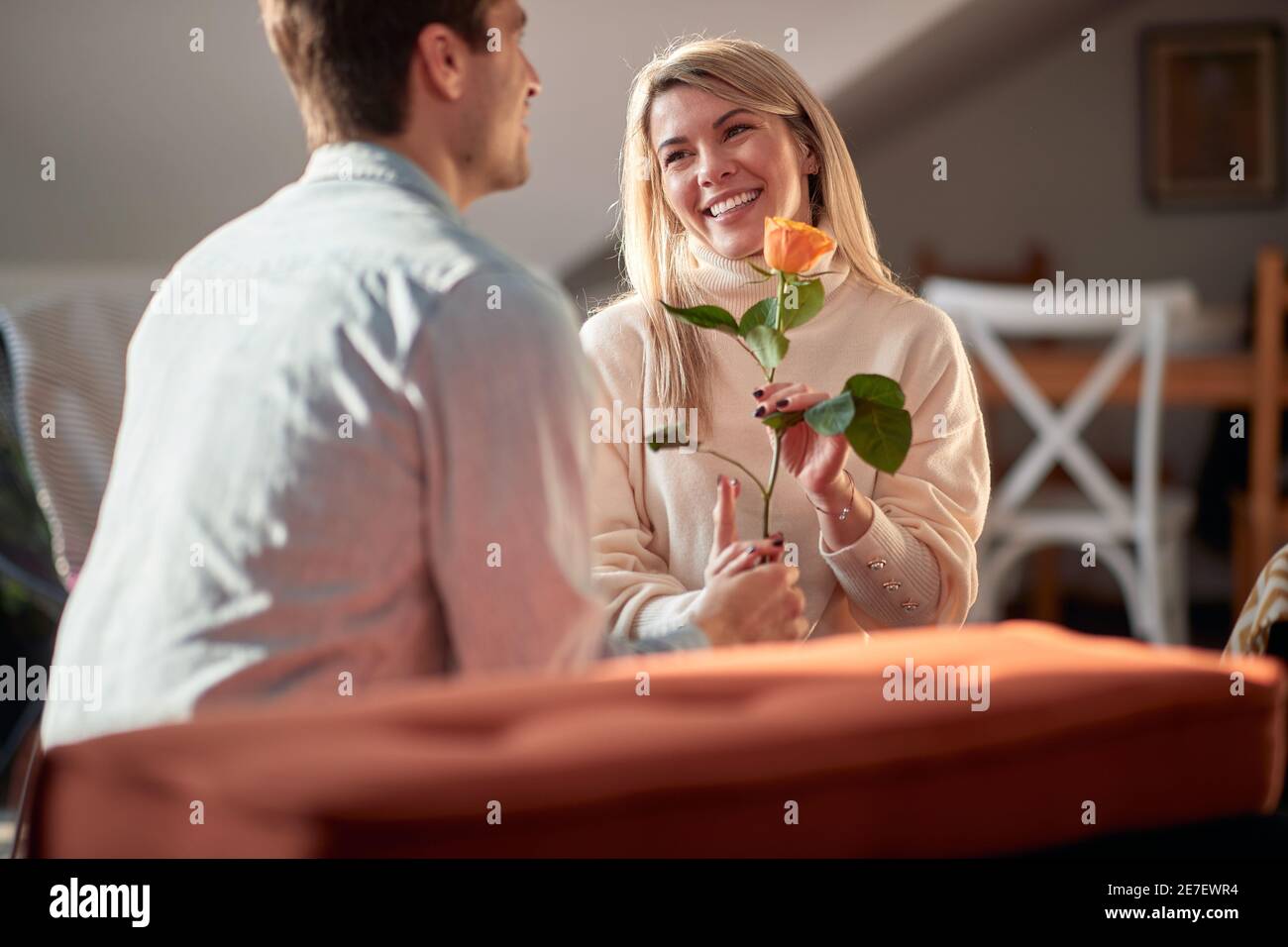 A young woman in a relaxed atmosphere at home touched by a rose she got ...