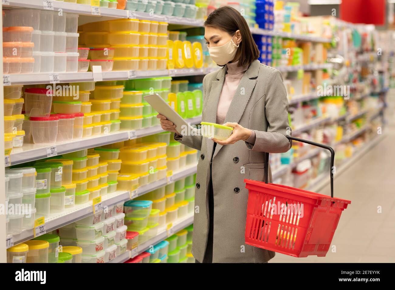 Young Asian female consumer with red shopping basket standing by large ...