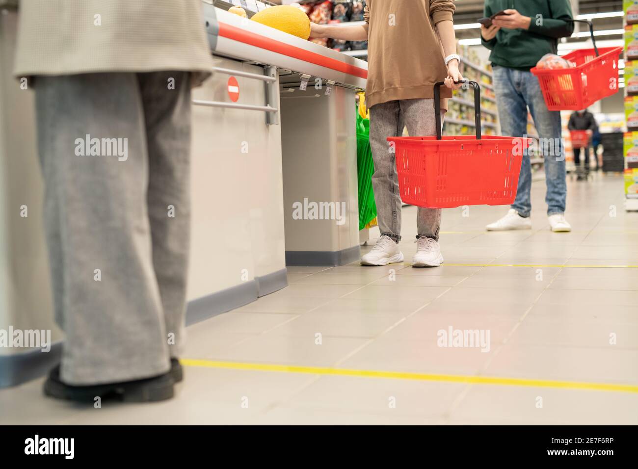 Low section of several customers with plastic shopping baskets standing ...