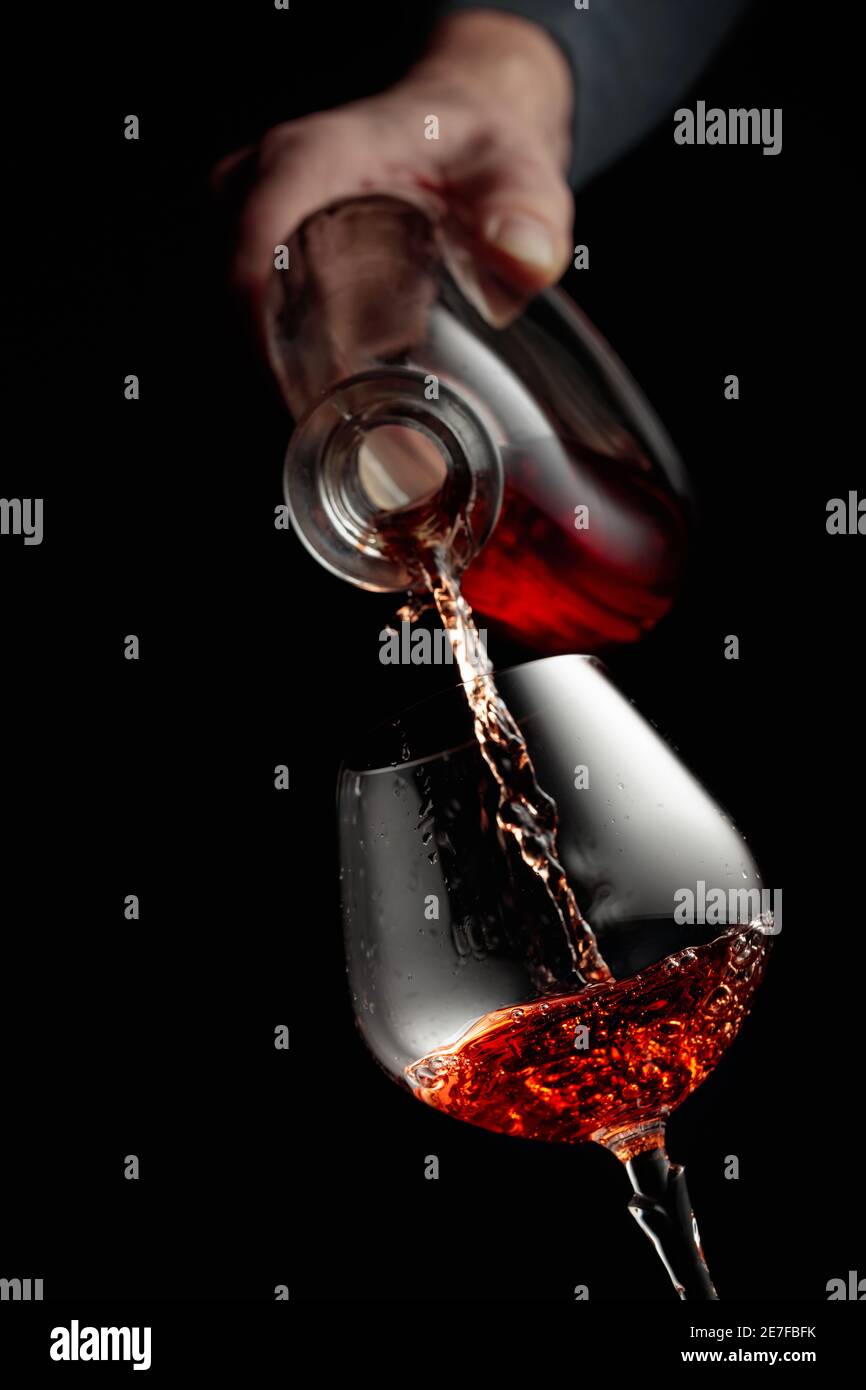 Pouring brandy in a glass goblet. Black background with copy space ...