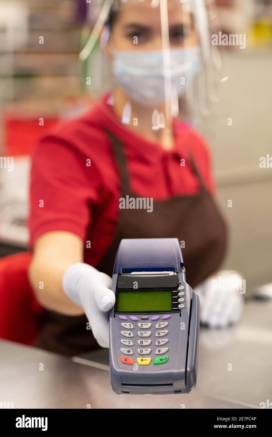 Gloved hand of female cashier in uniform, protective screen and mask ...