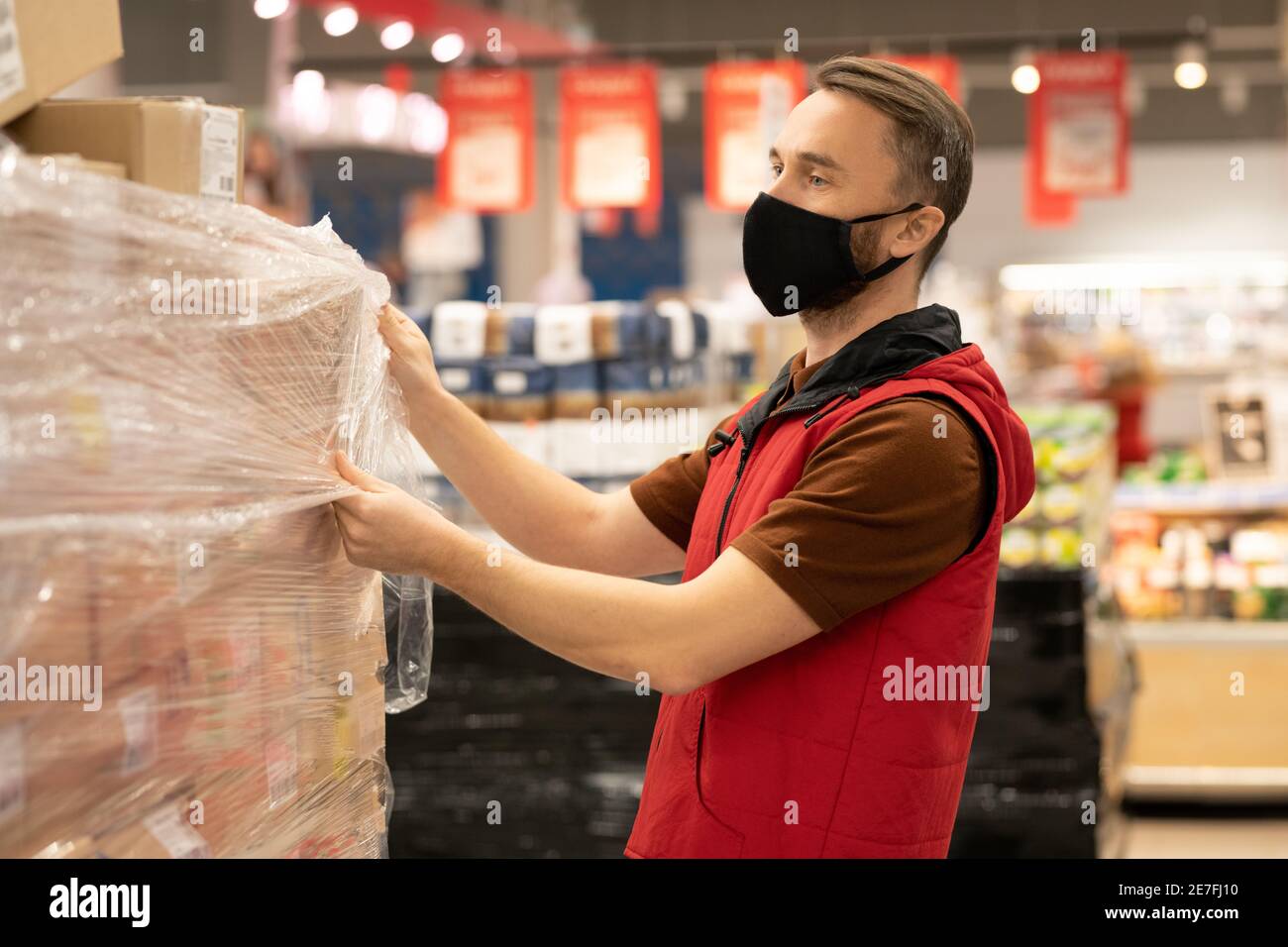 Young male worker of modern supermarket in uniform and protective mask ...