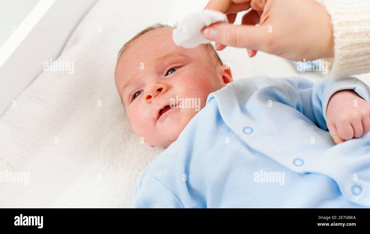 Closeup of mother cleaning face and eyes of her newborn baby son with ...