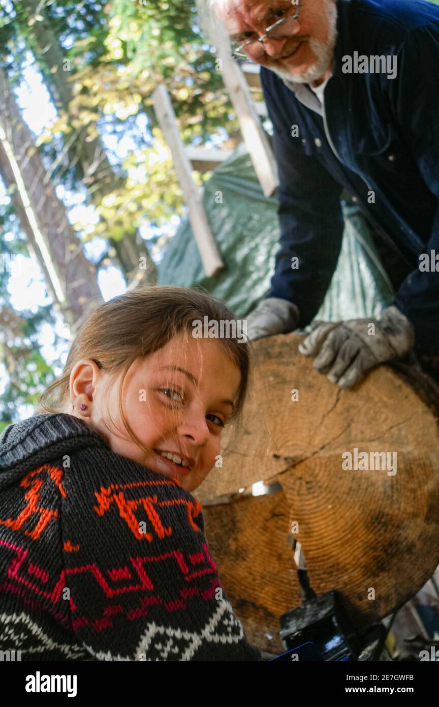 A young girl helping her grandfather to split logs using a mechanical ...