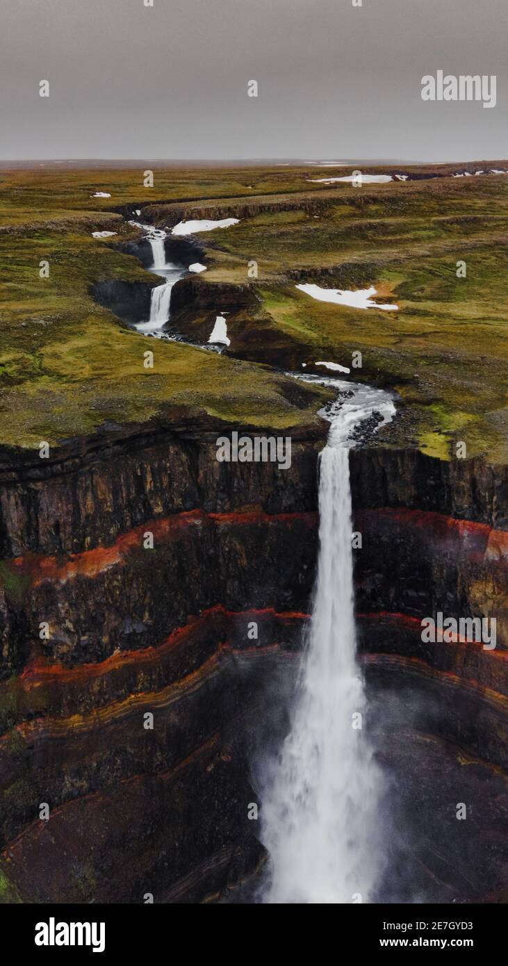 Vertical aerial shot of a waterfall in Iceland with textured rocks and ...