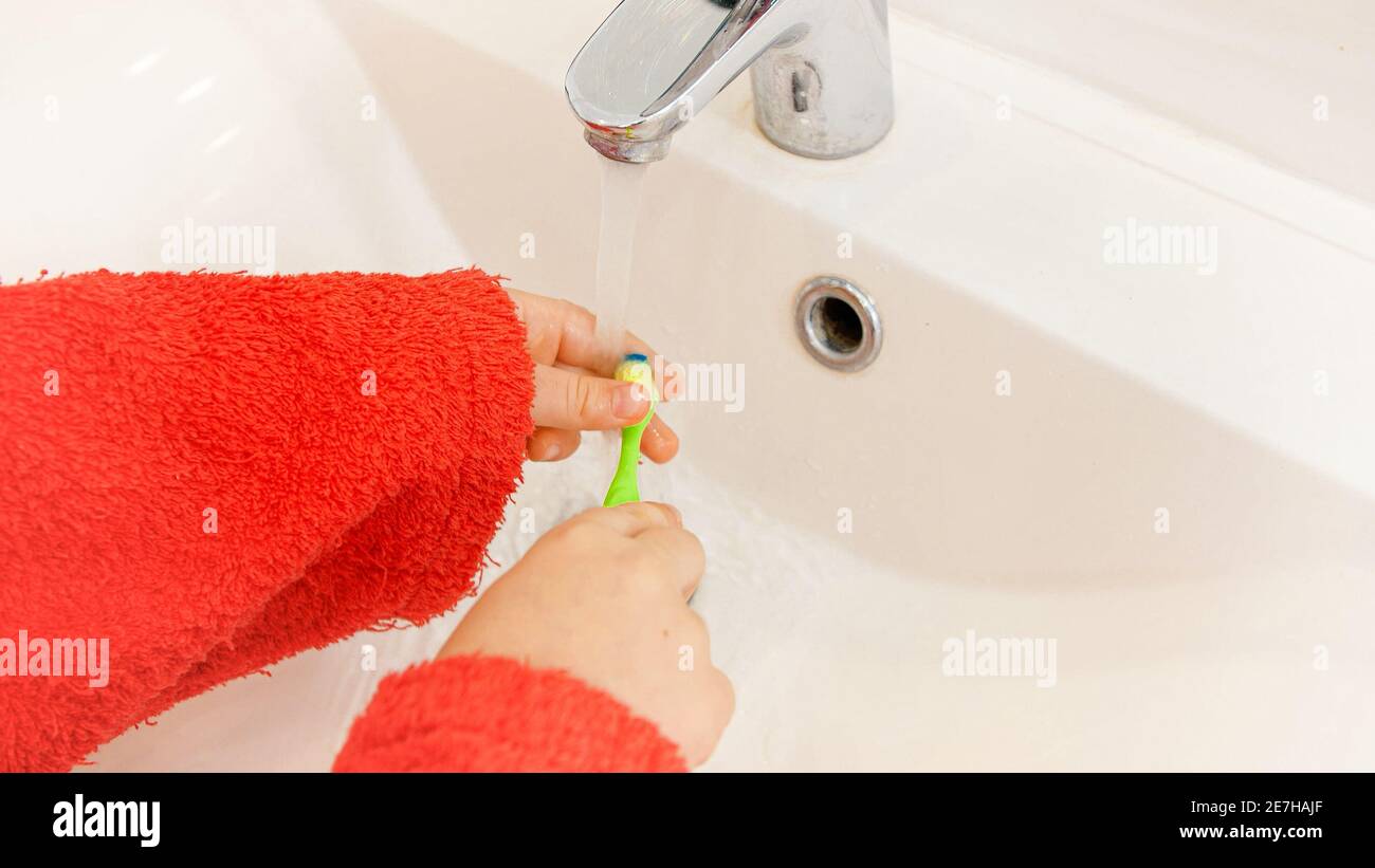 Closeup of little boy washing and cleaning toothbrush under water in ...