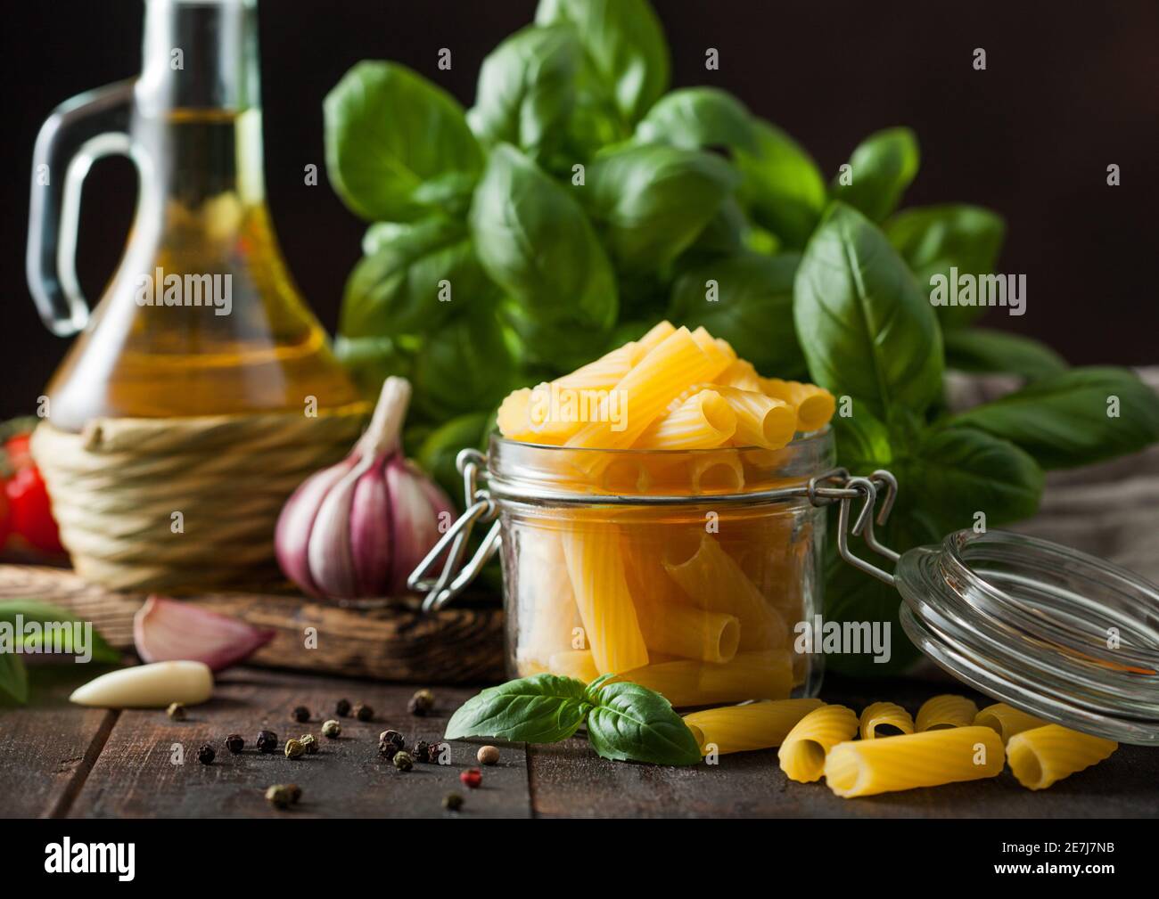 Glass jar of fresh raw penne pasta with oil and garlic, basil plant and ...