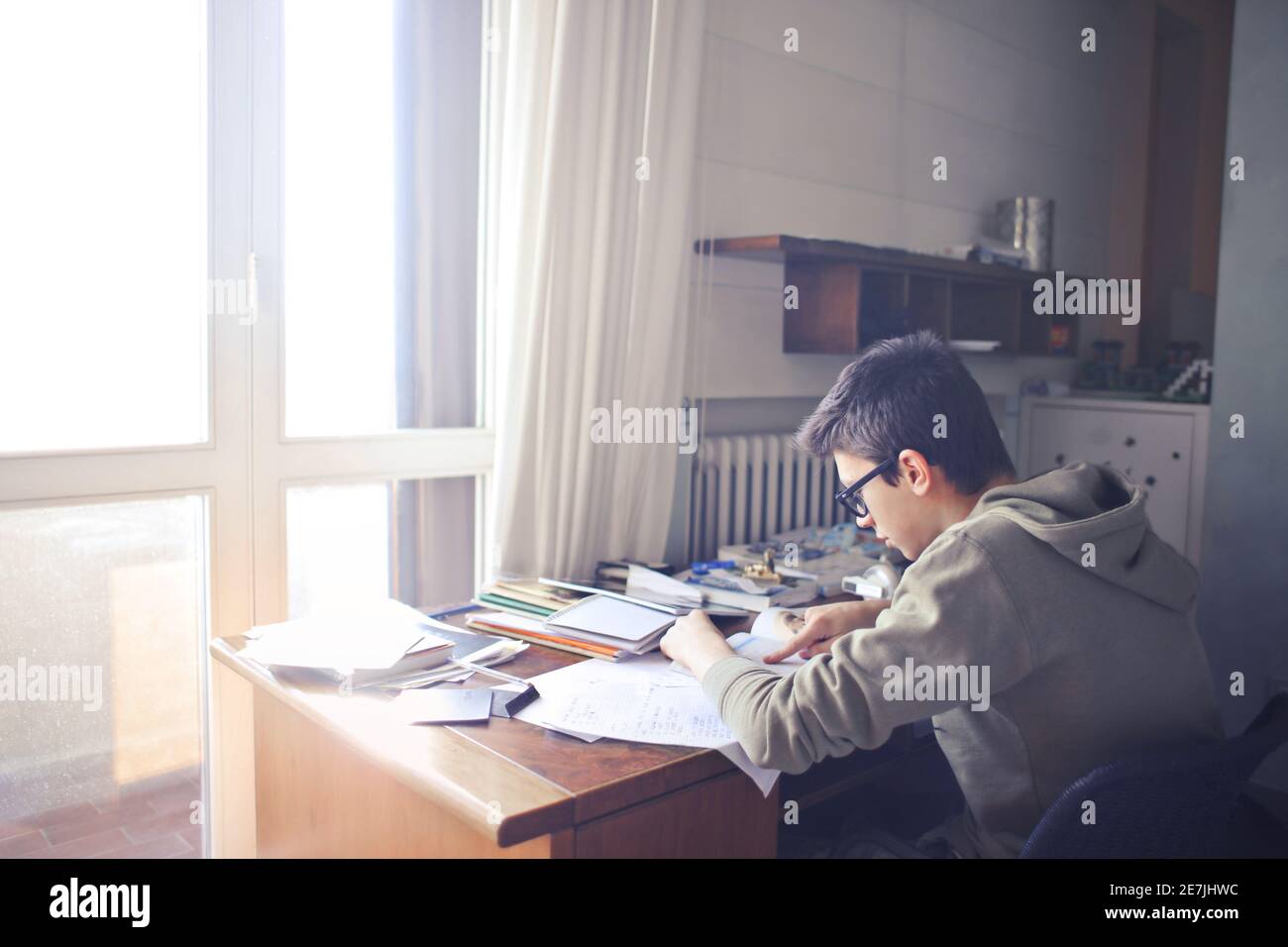 Boy with eyeglasses and a grey hoodie learning his lesson in his room ...