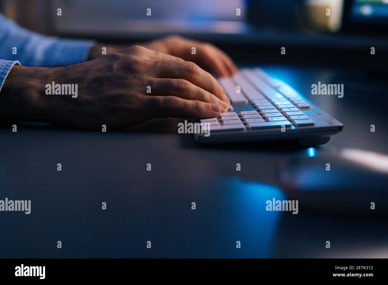 Side view of unrecognizable man typing online message using wireless keyboard at late night ...