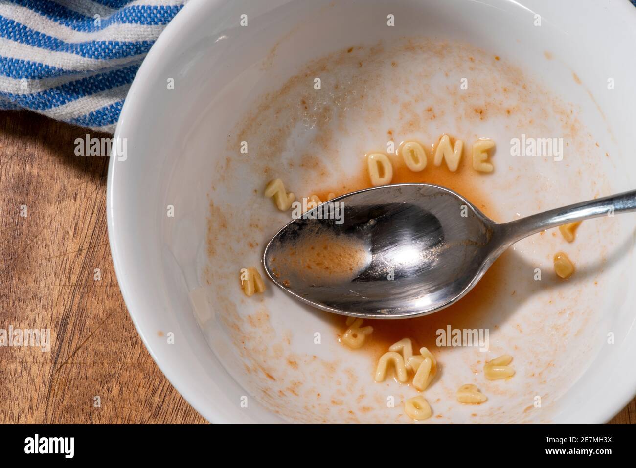 A spoon sits in nearly empty bowl of tomato alphabet soup, the noodles ...