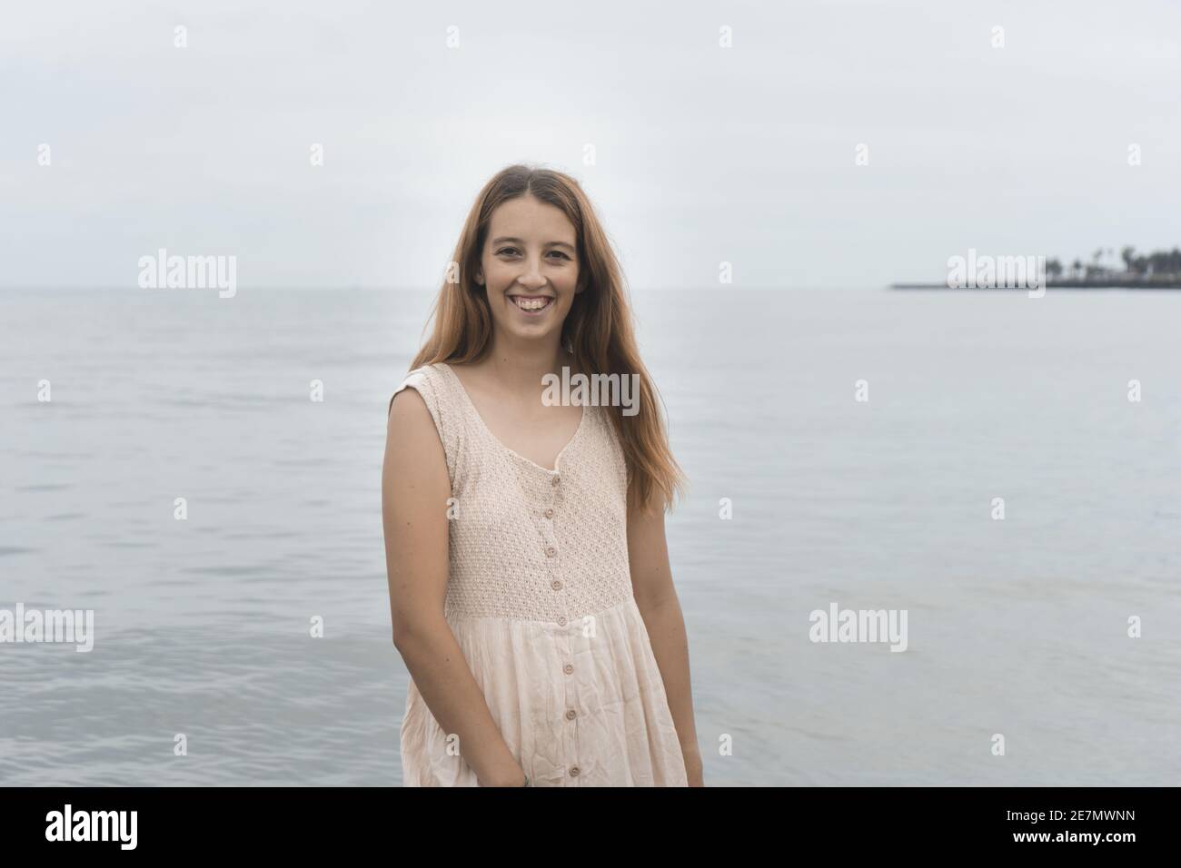 Happy Hispanic female in a beige sundress posing in the sea background ...